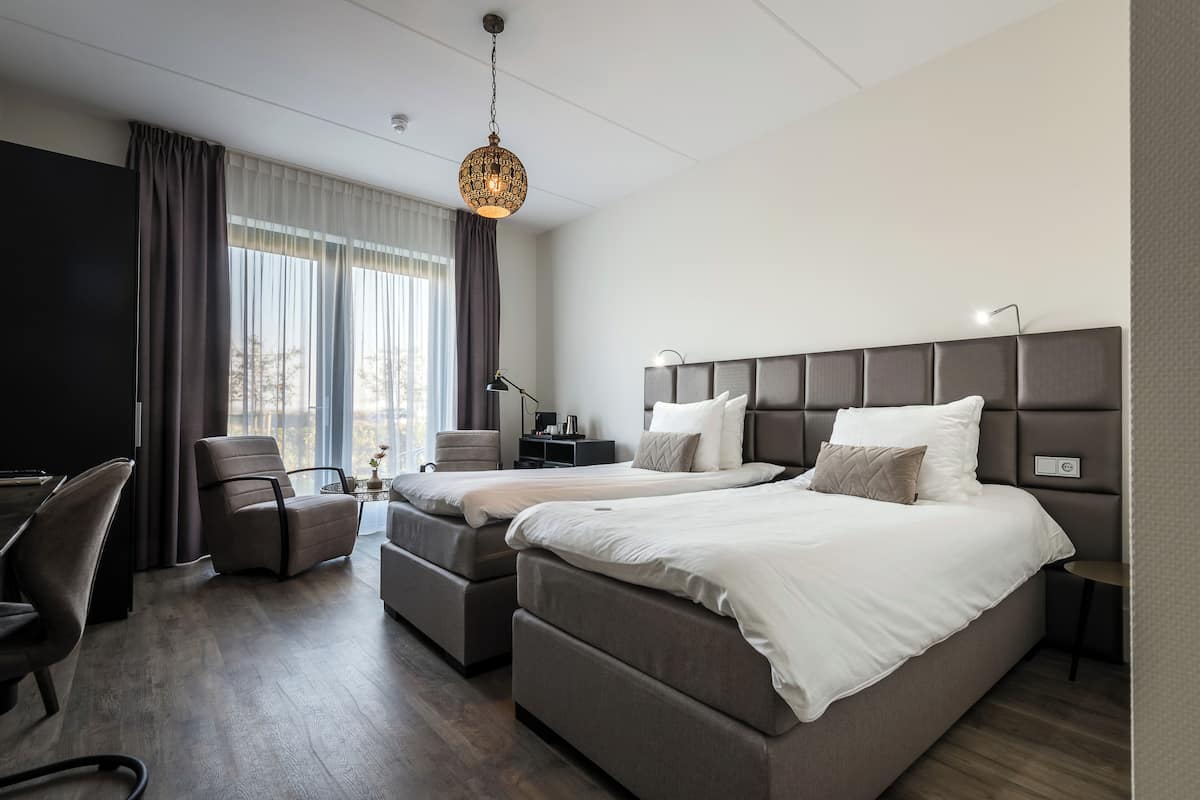Quarto de hotel moderno com duas camas, uma escrivaninha e uma cadeira.