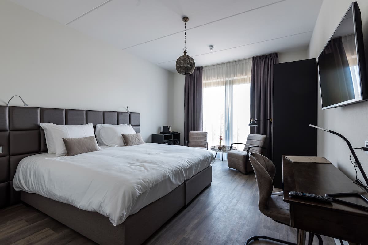 Quarto de hotel moderno com uma cama grande, uma escrivaninha, uma cadeira e uma televisão.