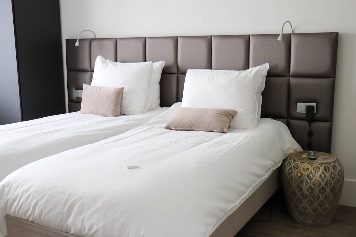 Uma cama de casal com cabeceira acolchoada, duas mesas de cabeceira e um vaso decorativo.