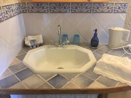 Uma pia de banheiro com uma torneira moderna, um dosador de sabão e um copo de água sobre o balcão.