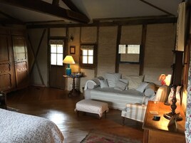 Um quarto aconchegante com piso de madeira, um sofá, uma mesa com abajur e uma cama com roupa de cama florida.