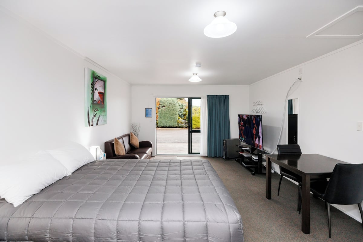 Quarto de hotel moderno com uma cama grande, uma escrivaninha, uma cadeira, uma televisão e vista para o exterior.