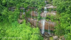 Uma cascata despenca sobre terreno rochoso, cercada por folhagem verde densa.