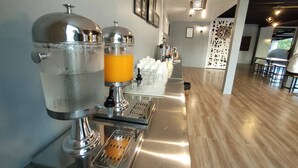 Balcão de pequeno-almoço com dispensadores de aço inoxidável, uma máquina de café e um tabuleiro com chávenas e copos.