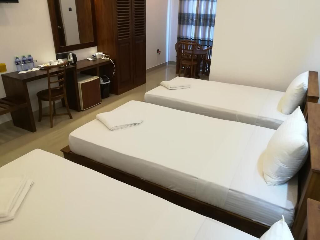 Quarto de hotel com duas camas individuais, uma escrivaninha com cadeira, uma mesinha e um espelho.
