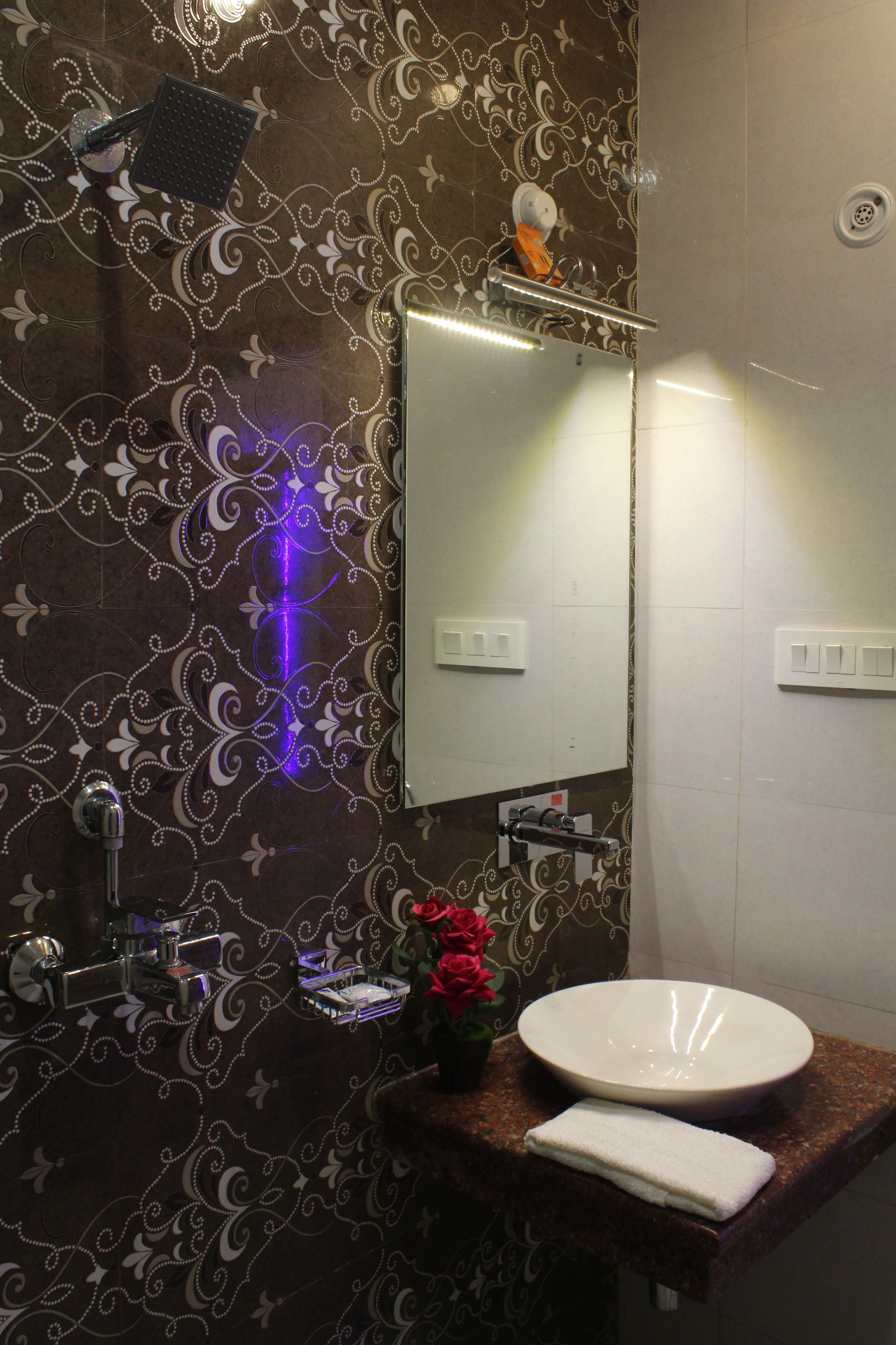 Um banheiro com revestimento de azulejos decorativos, uma pia redonda, um espelho e um porta-toalhas.