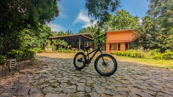Uma bicicleta estacionada em um caminho de pedras irregulares, em frente a um edifício com telhado de azulejos e uma fonte ao fundo.