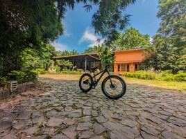 Uma bicicleta estacionada em um caminho de pedras irregulares, em frente a um edifício com telhado de azulejos e uma fonte ao fundo.