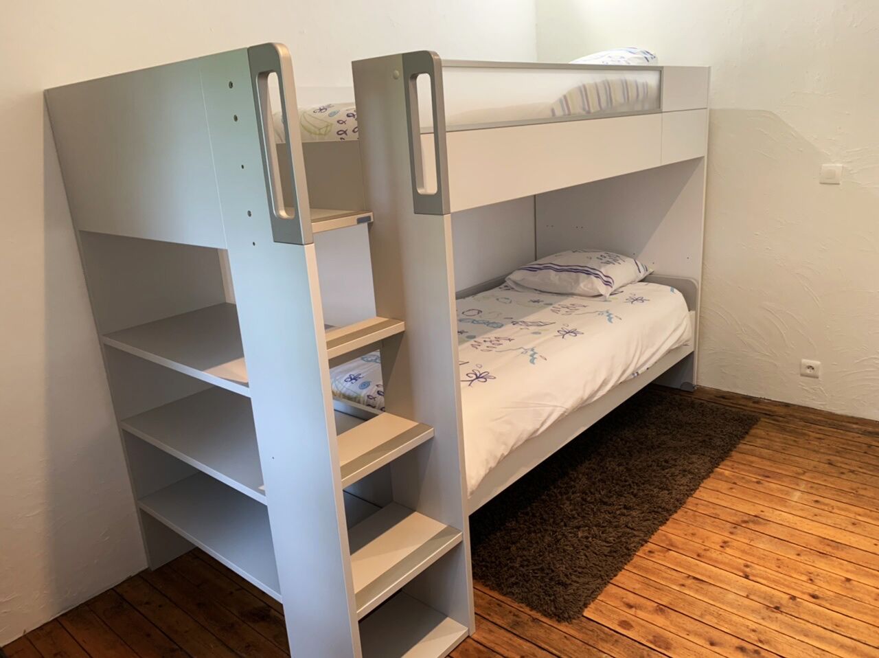 Uma cama beliche com escada, uma mesa de cabeceira e um pequeno armário.