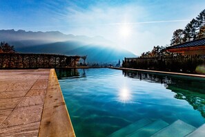 Piscina translúcida com deck de madeira e vista para montanhas ao fundo.
