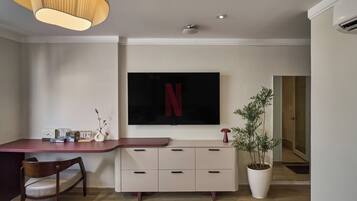 Uma sala de estar moderna com televisão de tela plana na parede, mesa de jantar de madeira com cadeiras, um vaso de planta e um armário embutido com gavetas.