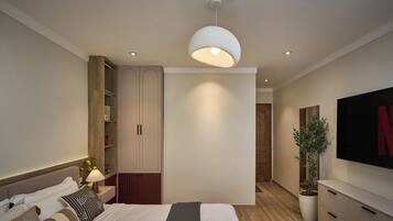 Quarto moderno com cama, mesa de cabeceira, luminária, guarda-roupa e TV fixada na parede.