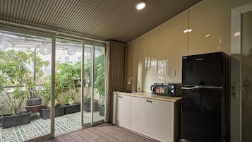 Cozinha moderna com geladeira preta, micro-ondas e pia. Uma porta de vidro deslizante dá acesso a um pátio com plantas em vasos.