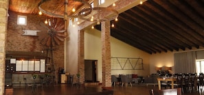 Espaçoso interior com paredes de tijolo aparente, teto de madeira maciça e uma estrutura central semelhante a um moinho. Há várias áreas de estar com mesas e cadeiras, além de um bar com design rústico.