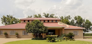 Um edifício de dois andares com telhado vermelho, rodeado por vegetação e árvores.