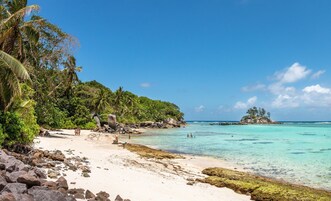 Uma praia tropical com águas turquesa cristalinas, margem rochosa e vegetação exuberante.