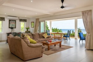 Uma sala de estar espaçosa com um sofá grande, uma mesa de centro e vista para o oceano através de grandes janelas.