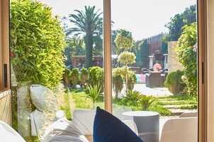 Vista de um quarto com uma janela grande, dando para um jardim com diversas plantas e área de piscina.