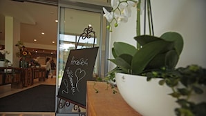 Uma área de recepção com placa de boas-vindas, um vaso de planta e vista para o interior.