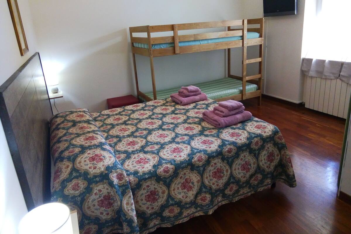 Quarto com cama de solteiro, colcha estampada, mesa de cabeceira pequena e televisão na parede.