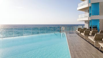 Uma área à beira da piscina com vista para o oceano, cadeiras de espreguiçadeira e um salva-vidas.
