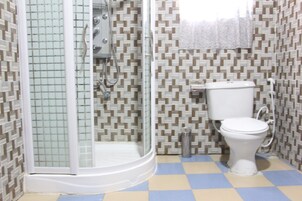 Casa de banho com chuveiro, sanita e paredes com azulejos estampados.