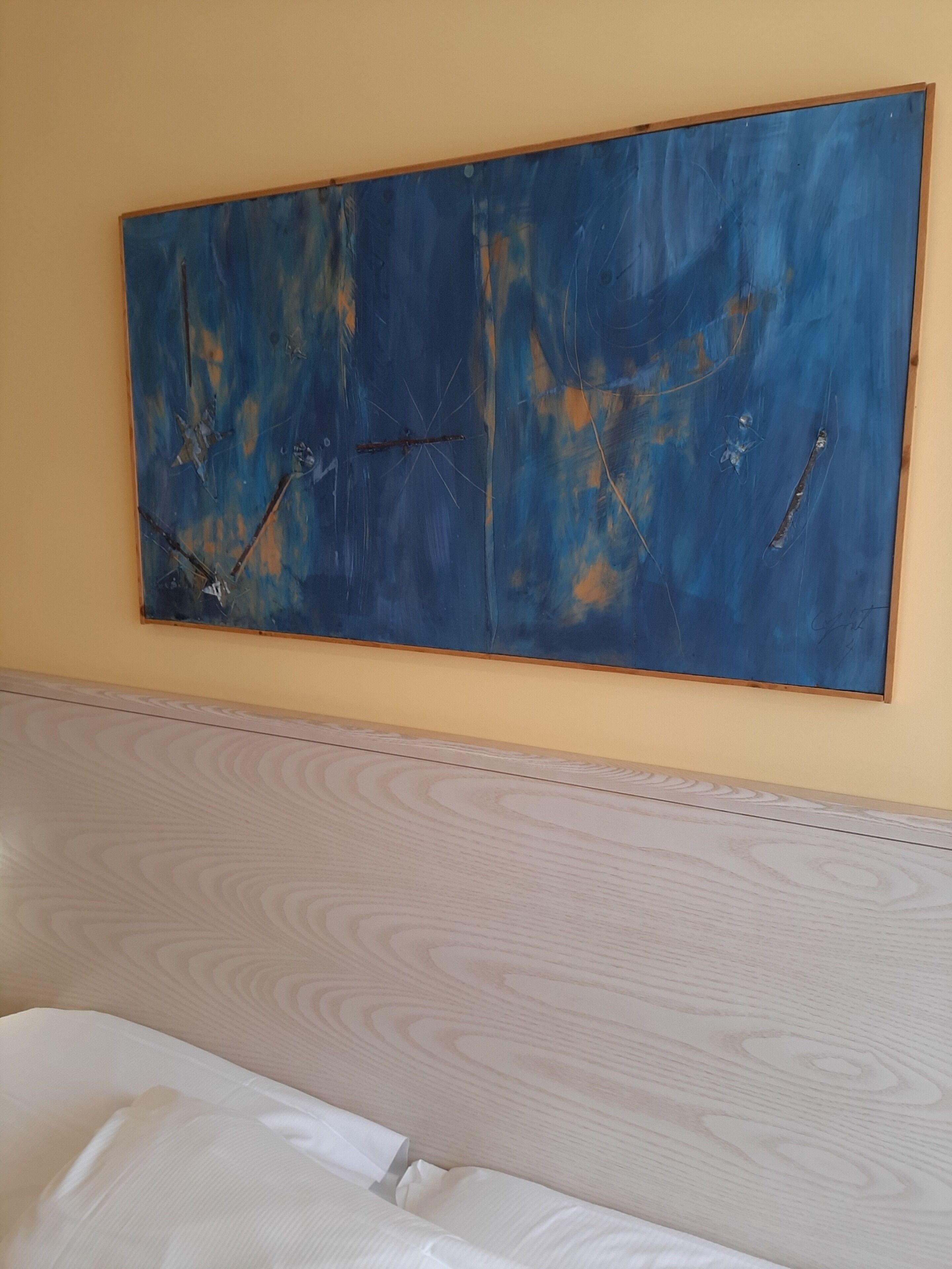 Quarto com uma cama, cabeceira e uma grande pintura abstrata na parede.