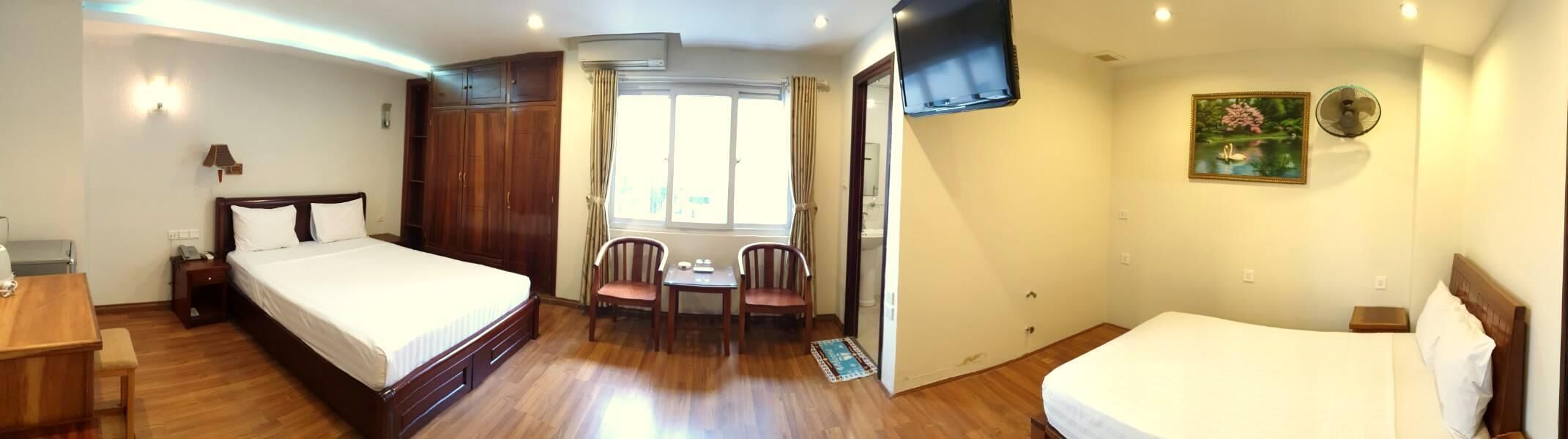 Quarto de hotel com duas camas, uma escrivaninha, uma cadeira, uma mesinha, televisão e janela com cortinas.