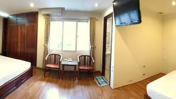 Quarto de hotel com duas camas, uma escrivaninha, uma cadeira, uma mesinha, televisão e janela com cortinas.