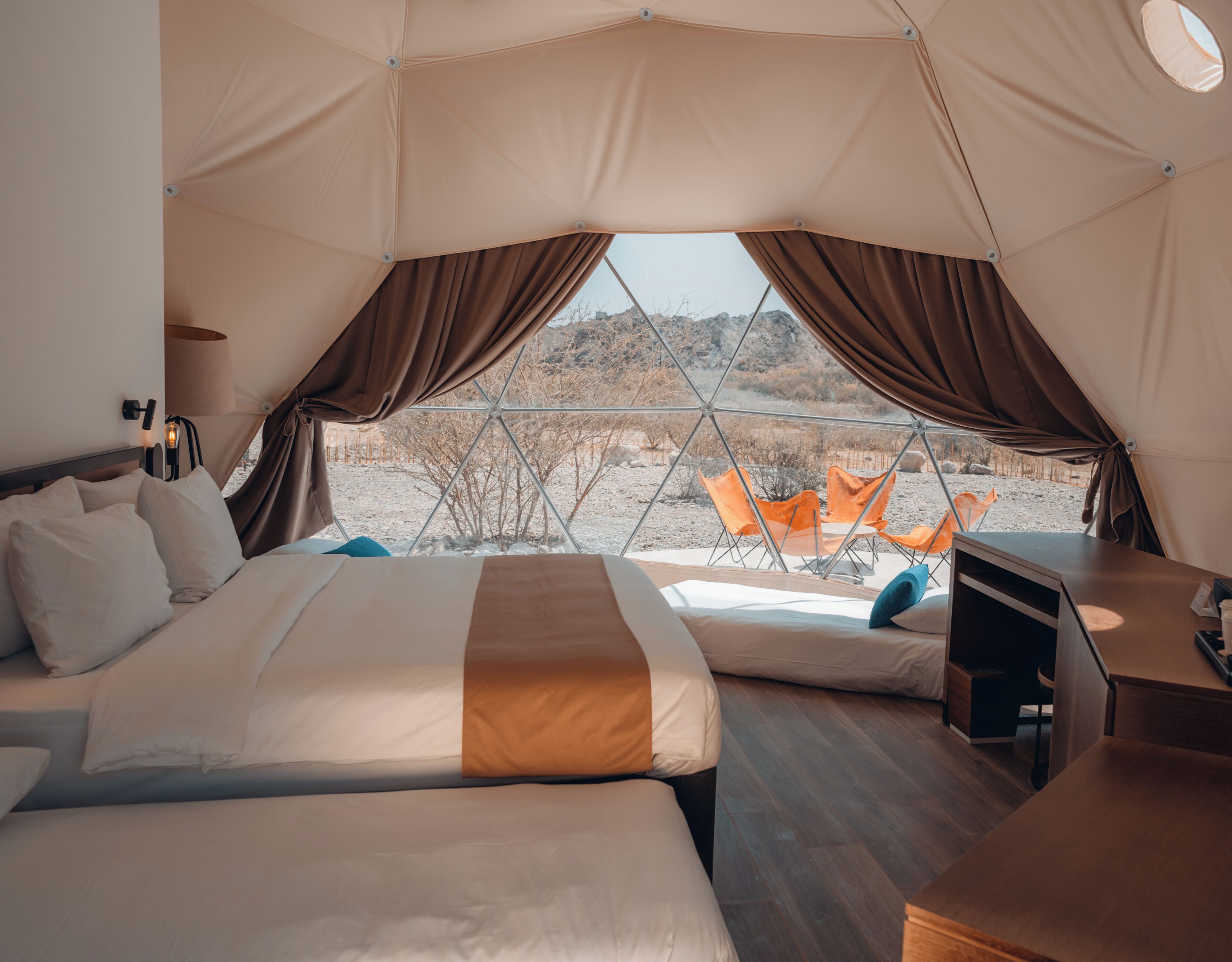 Quarto de acomodação em tenda com cama, escrivaninha e vista para o exterior.