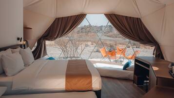 Quarto de acomodação em tenda com cama, escrivaninha e vista para o exterior.