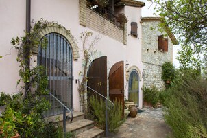Um edifício com portas em arco, uma parede de pedra e uma escadaria que leva a uma varanda.