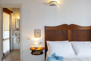 Quarto com cabeceira de madeira, mesa de cabeceira com abajur, quadro emoldurado na parede e janela com cortinas.