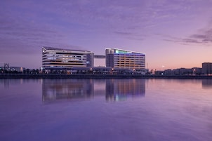 Um hotel moderno com vários andares e varandas, localizado à beira de um corpo de água.