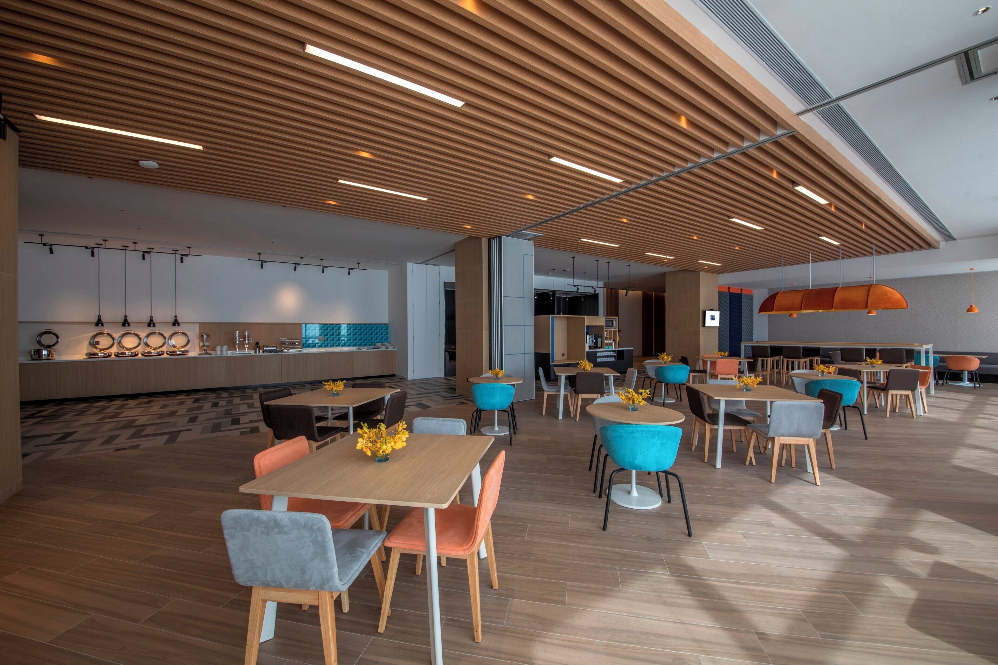 Uma sala de jantar moderna com ripas de madeira no teto, várias mesas e cadeiras.
