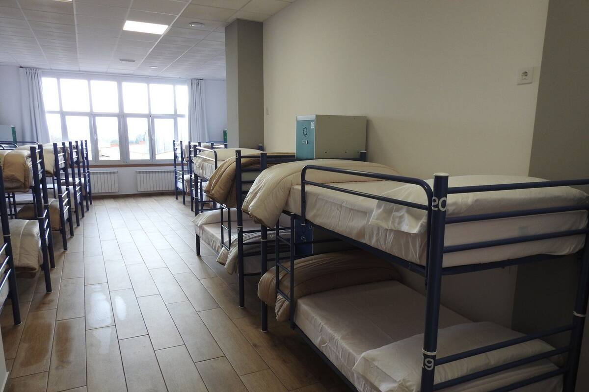 Um dormitório com beliches, um radiador e uma janela com cortinas.