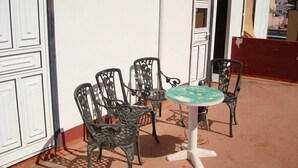 Pátio externo com quatro cadeiras de metal e uma mesa redonda pequena.