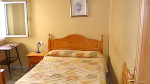 Quarto com cama de madeira, mesa de cabeceira com abajur, cadeira e espelho na parede.