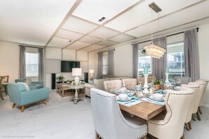 Uma sala de estar ampla com um sofá, uma mesa de jantar posta para seis pessoas e uma televisão.