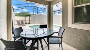 Uma área de varanda coberta com mesa e cadeiras de vidro, piscina e vista para o exterior.