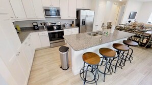 Cozinha moderna com armários brancos, eletrodomésticos de aço inoxidável, bancada de granito e um espaço de bar com banquetas.