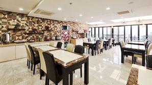 Uma área de refeições moderna com várias mesas e cadeiras, cozinha equipada e amplas janelas com vista.