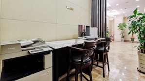 Uma mesa de recepção com uma impressora Canon, um computador e uma placa de identificação. Há duas cadeiras de madeira e um vaso com planta.
