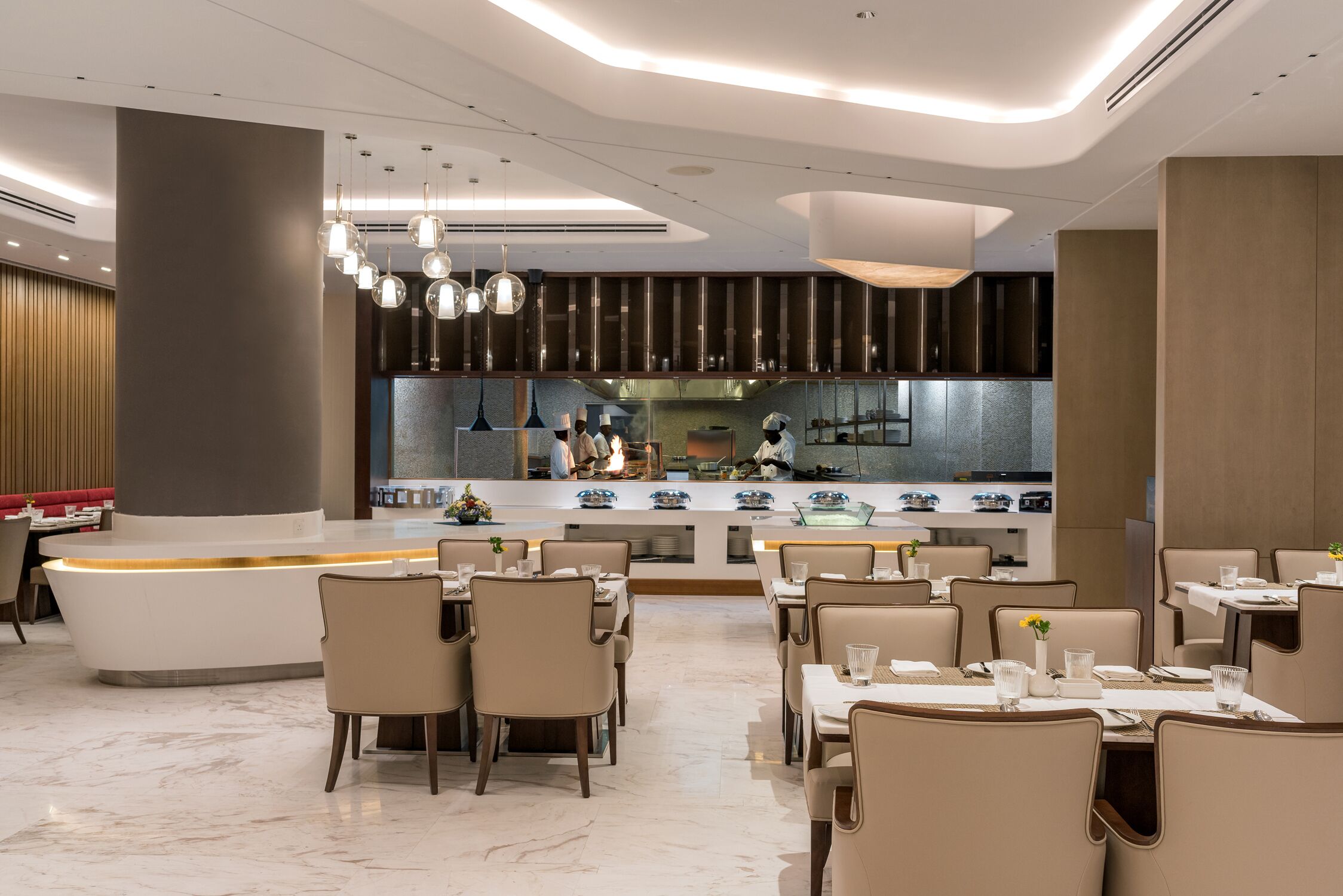 Restaurante moderno com área de bar central, diversas mesas de jantar e cozinha ao fundo.