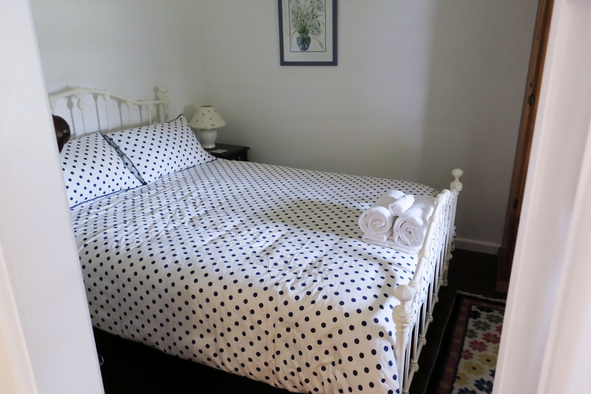 Cama bem arrumada com colcha de bolinhas, travesseiro branco e toalhas enroladas ao lado.