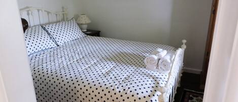 Cama bem arrumada com colcha de bolinhas, travesseiro branco e toalhas enroladas ao lado.
