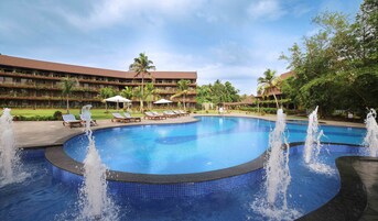 Piscina de hotel com jatos de água, espreguiçadeiras e guarda-sóis.