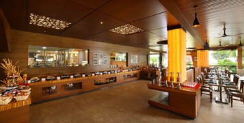 Um hall de hotel espaçoso com um longo balcão de buffet, área de estar com mesas e cadeiras, e uma grande janela com vista para o exterior.