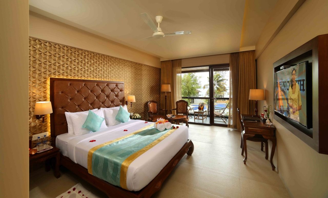 Quarto de hotel com uma cama grande, ventilador de teto, televisão e vista para o exterior.