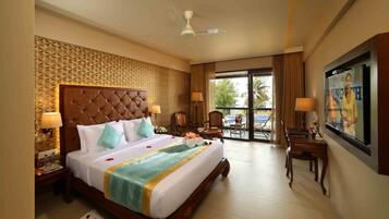 Quarto de hotel com uma cama grande, ventilador de teto, televisão e vista para o exterior.